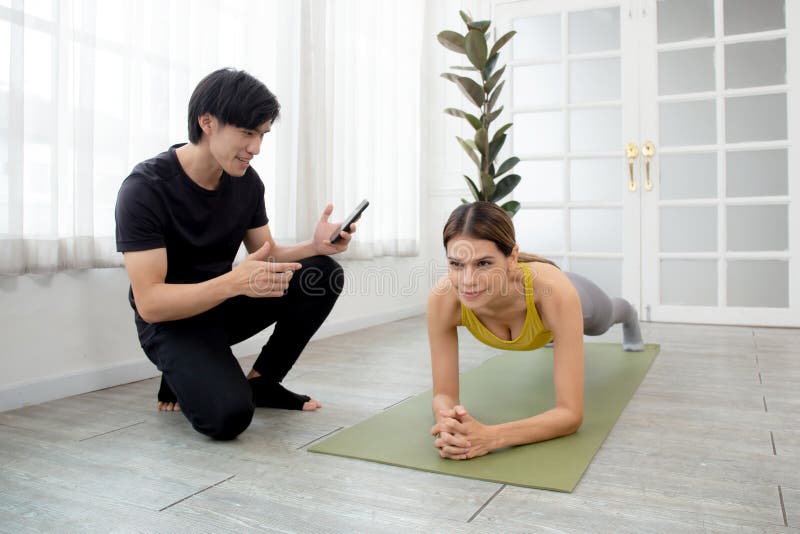 Young Woman Practicing Workout with Posture Plank while Man Coach Determination Time for Doing ...
