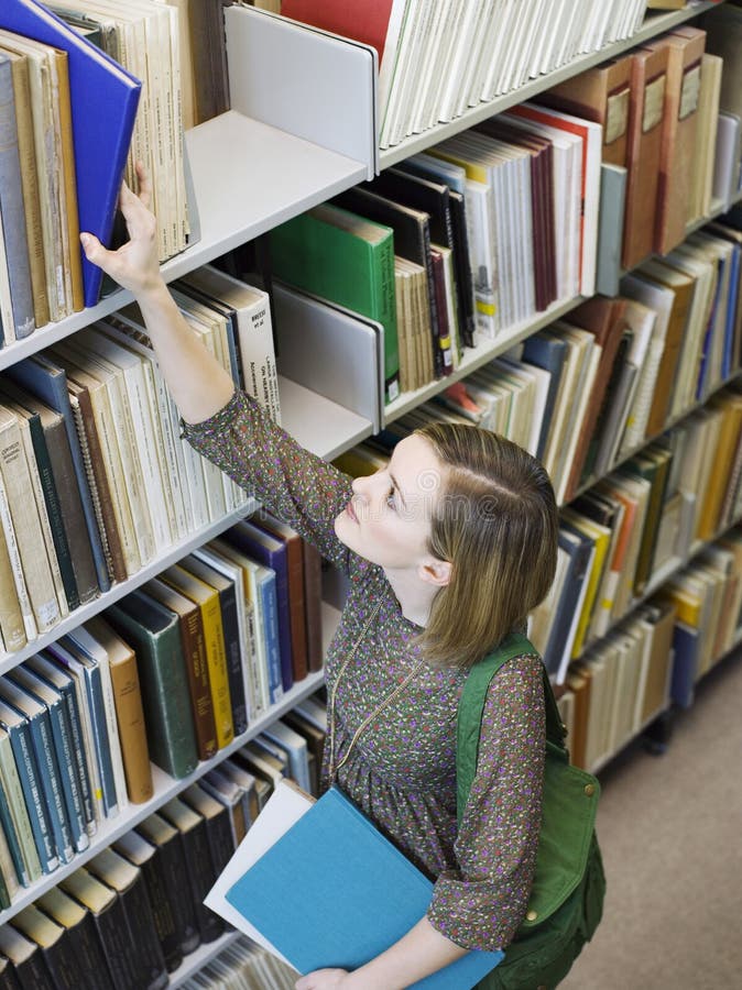 Young Woman Reaching for Book from Library Shelf Stock Image - Image of ...