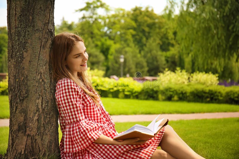 Young Woman Reading Book While Sitting Near Tree In Park Stock Image