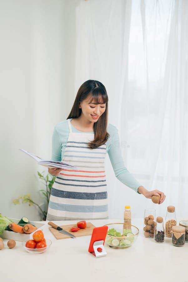 Young Woman Reading Cookbook in the Kitchen, Looking for Recipe Stock ...