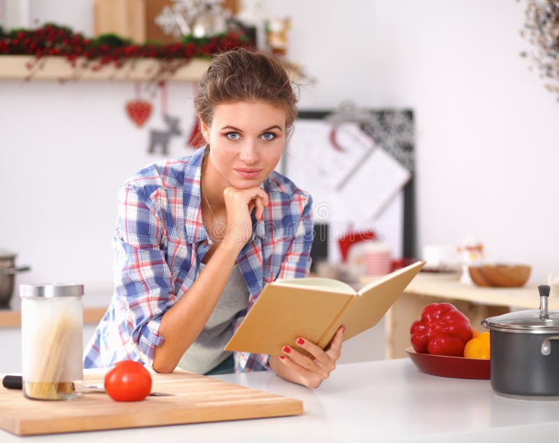 Young Woman Reading Cookbook in the Kitchen, Looking for Recipe Stock ...