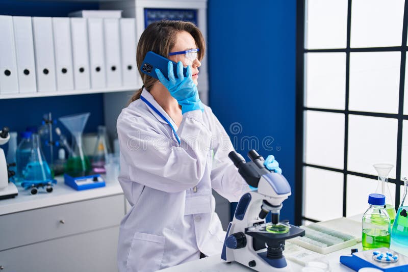 Young Woman Scientist Using Microscope Talking on Smartphone at ...