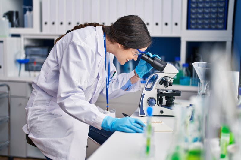 Young Woman Scientist Writing on Notebook Using Microscope at ...