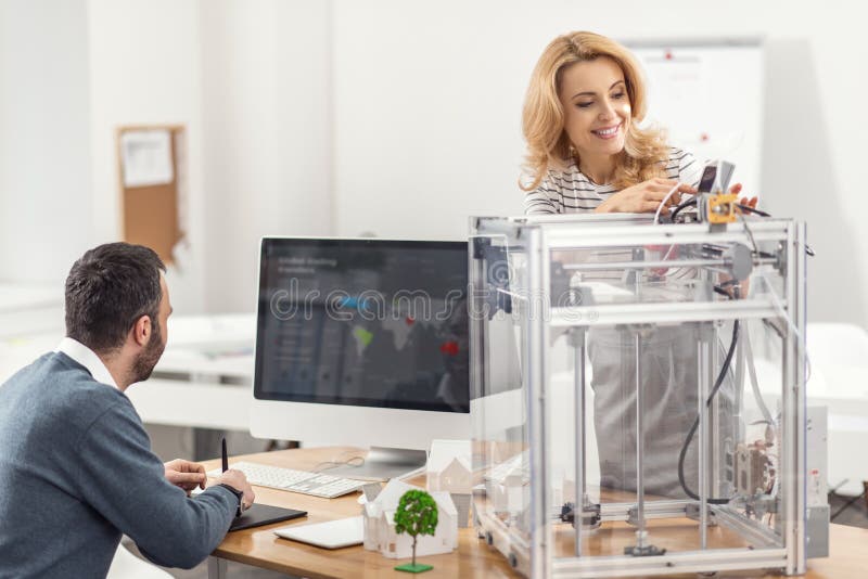 Young Woman Setting Up 3D Printer while Man Creating Presentation Stock ...