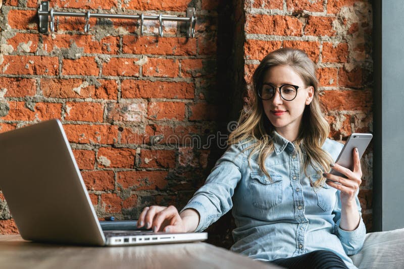 Young Woman Sits in Cafe on Windowsill, Holding Smartphone while Using ...