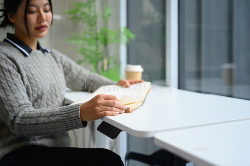 Young Woman Sitting at a Desk in a Modern Office and Reading Book Stock ...
