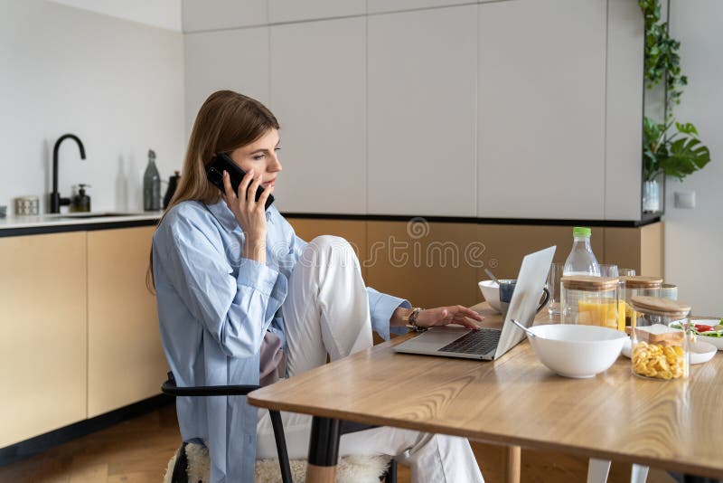 Young Woman Sitting at Kitchen Table Using Laptop Computer and Talking ...