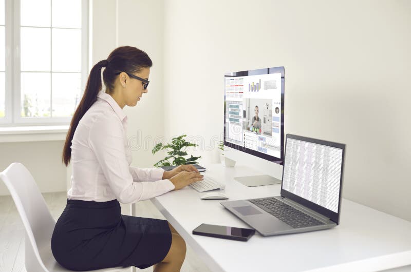 Young Woman Sitting at Office Desk, Using Multiple Computers and ...