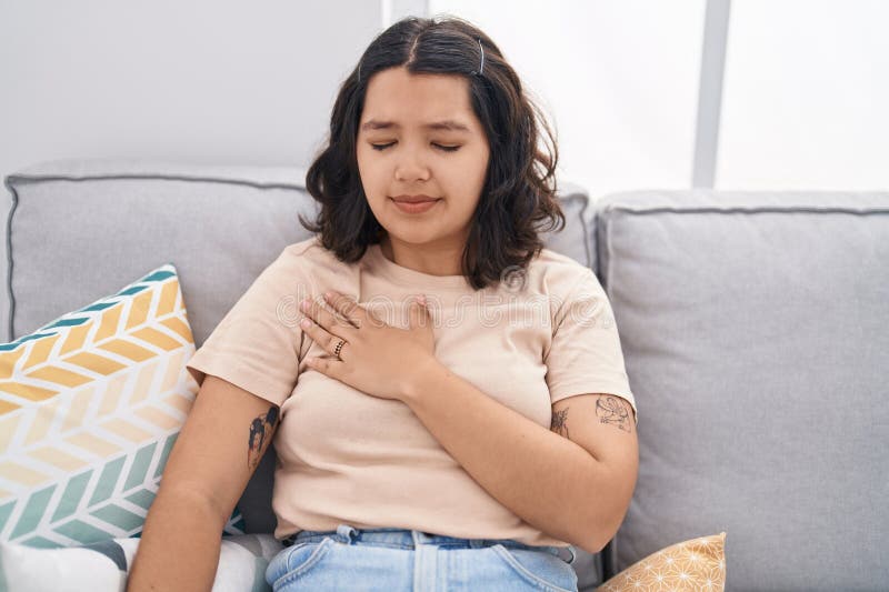 Young Woman Sitting on Sofa Touching Chest at Home Stock Photo - Image ...