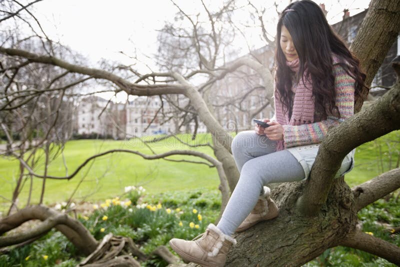 Young Woman Sitting on Tree Branch while Text Messaging Stock Image ...
