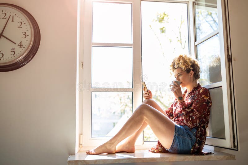 Young Woman Sitting on Window Sill and Using Smartphone Stock Image ...