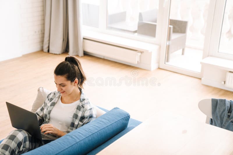 Young Woman Smiling and Using Laptop while Resting on Couch Stock Photo ...