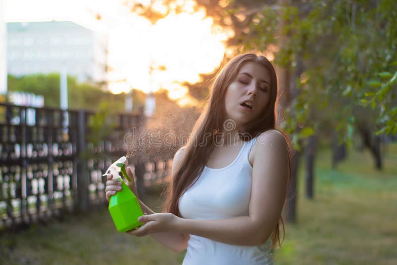 Young Woman Spraying Water on Herself from a Spray Bottle in a Summer ... Young Woman Spraying Water on Herself from a Spray Bottle in a Summer ...