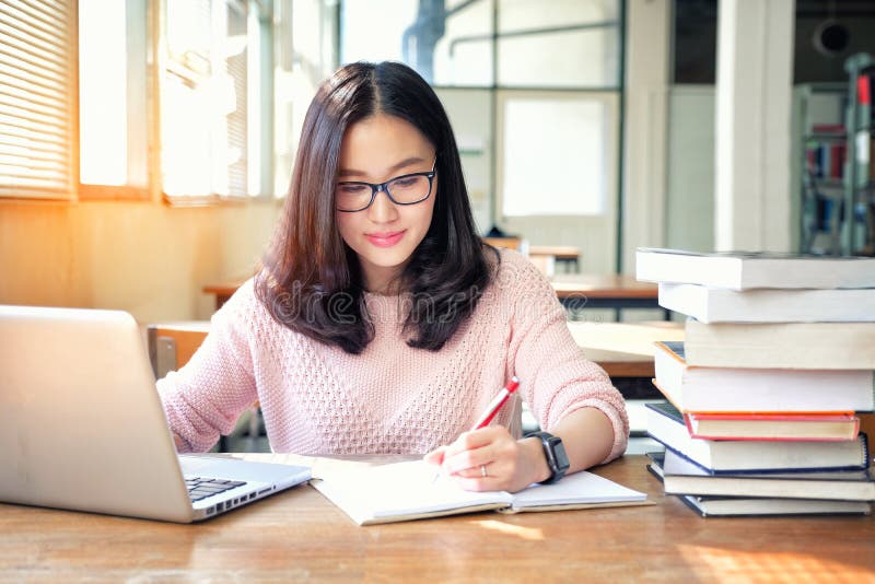Young Woman Taking Note and Using Laptop while Studying in Library ...