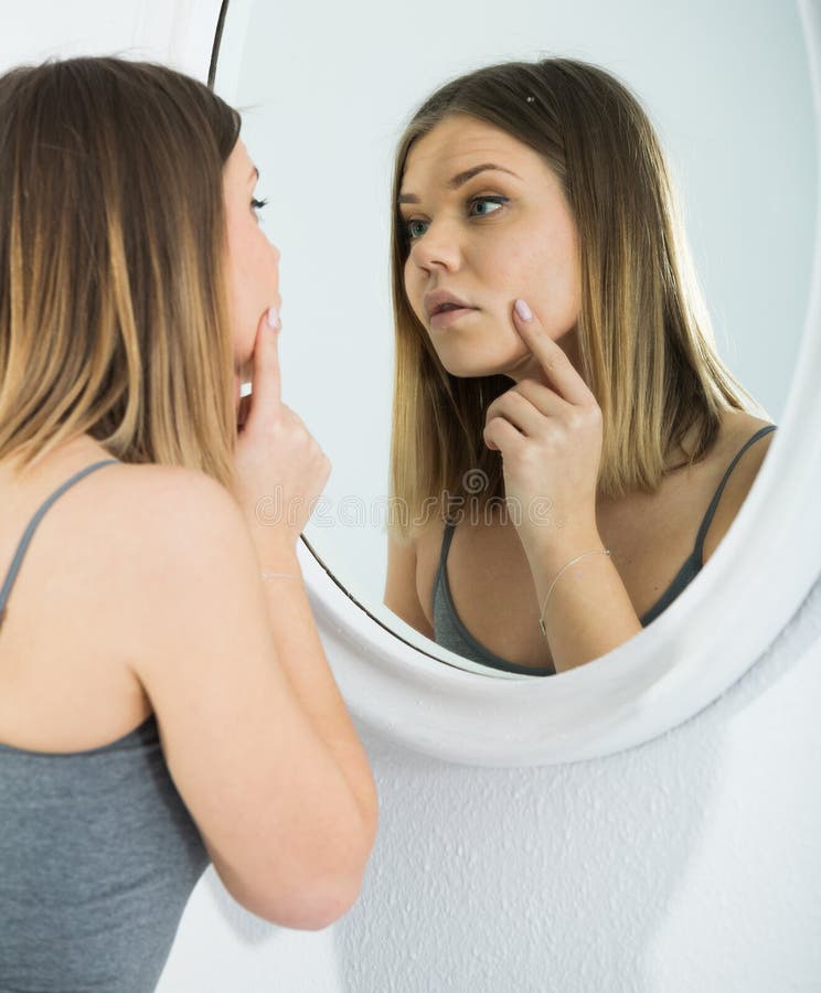 Young Woman Using Mirror and Touching Face in Bedroom Stock Image ...