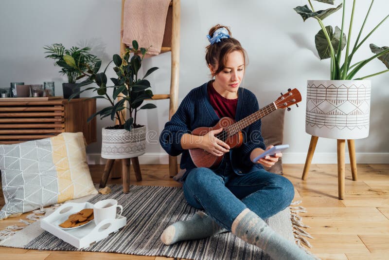 Young Woman Using Mobile Phone while Playing Ukulele Guitar in Modern ...