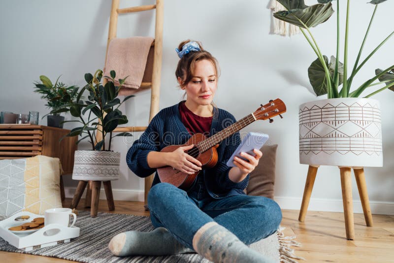 Young Woman Using Mobile Phone while Playing Ukulele Guitar in Modern ...