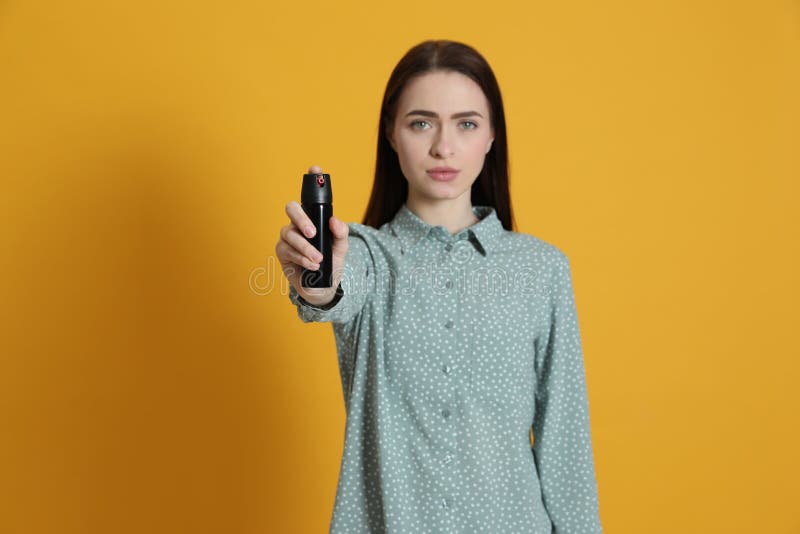 Young Woman Using Pepper Spray on Yellow Background Stock Photo - Image ...