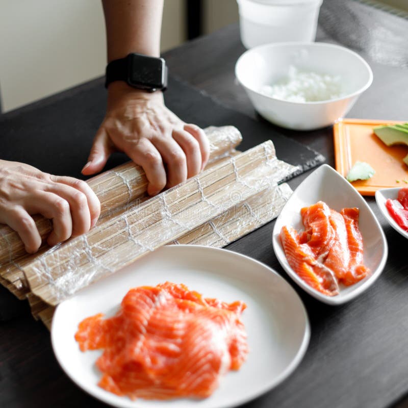 Young Woman Wrapping Up Sushi Roll Ingredients on Bamboo Mat Stock ...