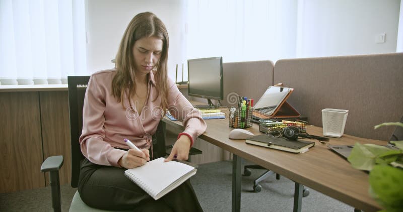 Young Woman Writing Notes in an Office, Showcasing a Professional ...