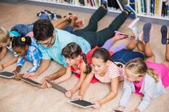 Teacher And Kids Lying On Floor Using Digital Tablet In Library Stock ...