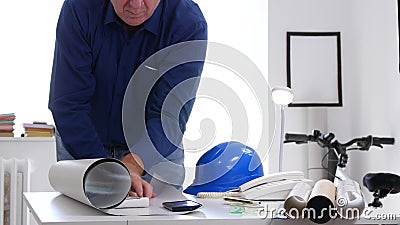 Busy Engineer in Interior Office Open and Analyze a Building Plan on ...