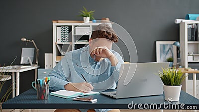 Exhausted Young Man Writing and Working with Computer Indoors at Work ...
