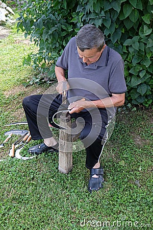 Farmer With Hammer And Iron Tool On The Tree Stump Is Sharpening His ...