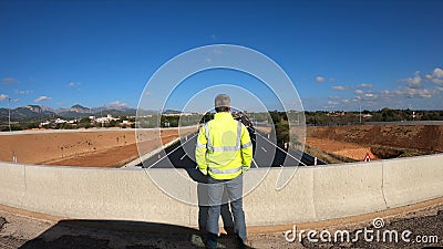 Rear View of a Man in a Yellow Safety Jacket Standing from a Bridge ...