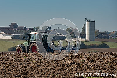 Tractor Ploughing Field With Blurry Farm In The Background Royalty-Free ...