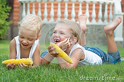 Two Brothers Lying On The Grass And Eat Corn On The Cob In The Garden ...
