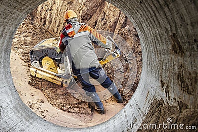 A Worker Compacts Soil Or Sand With A Vibrating Plate In A Trench At A ...