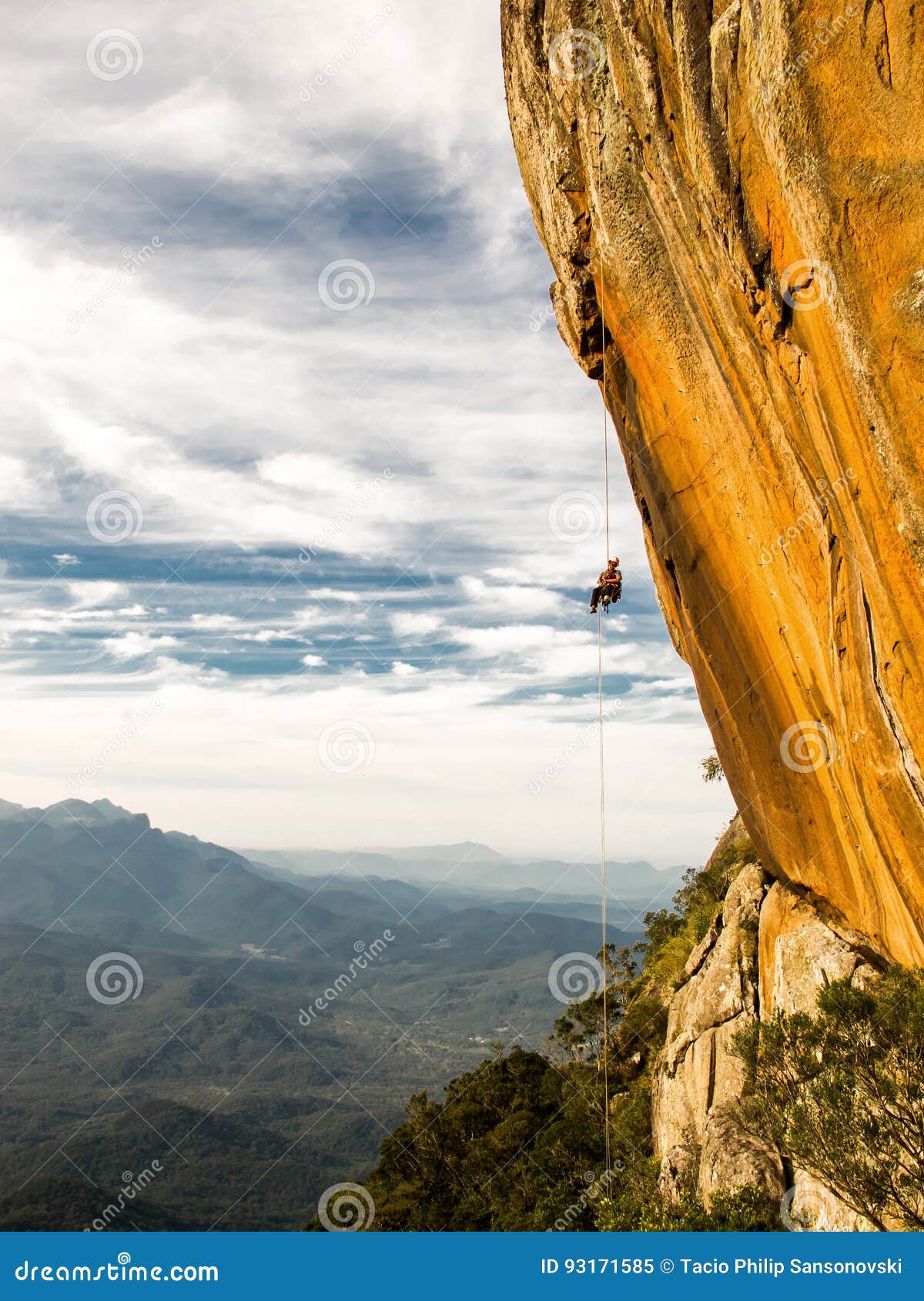 Abseiling a Negative Yellow Rock Wall with Mountains on Background ...