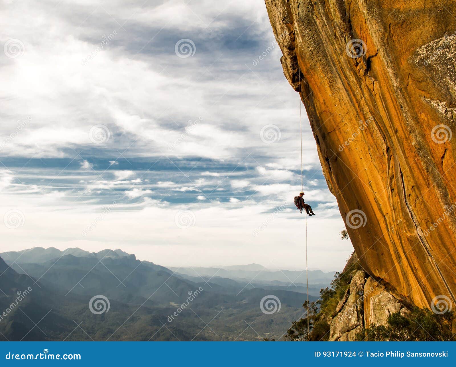 Abseiling a Negative Yellow Rock Wall with Mountains on Background ...