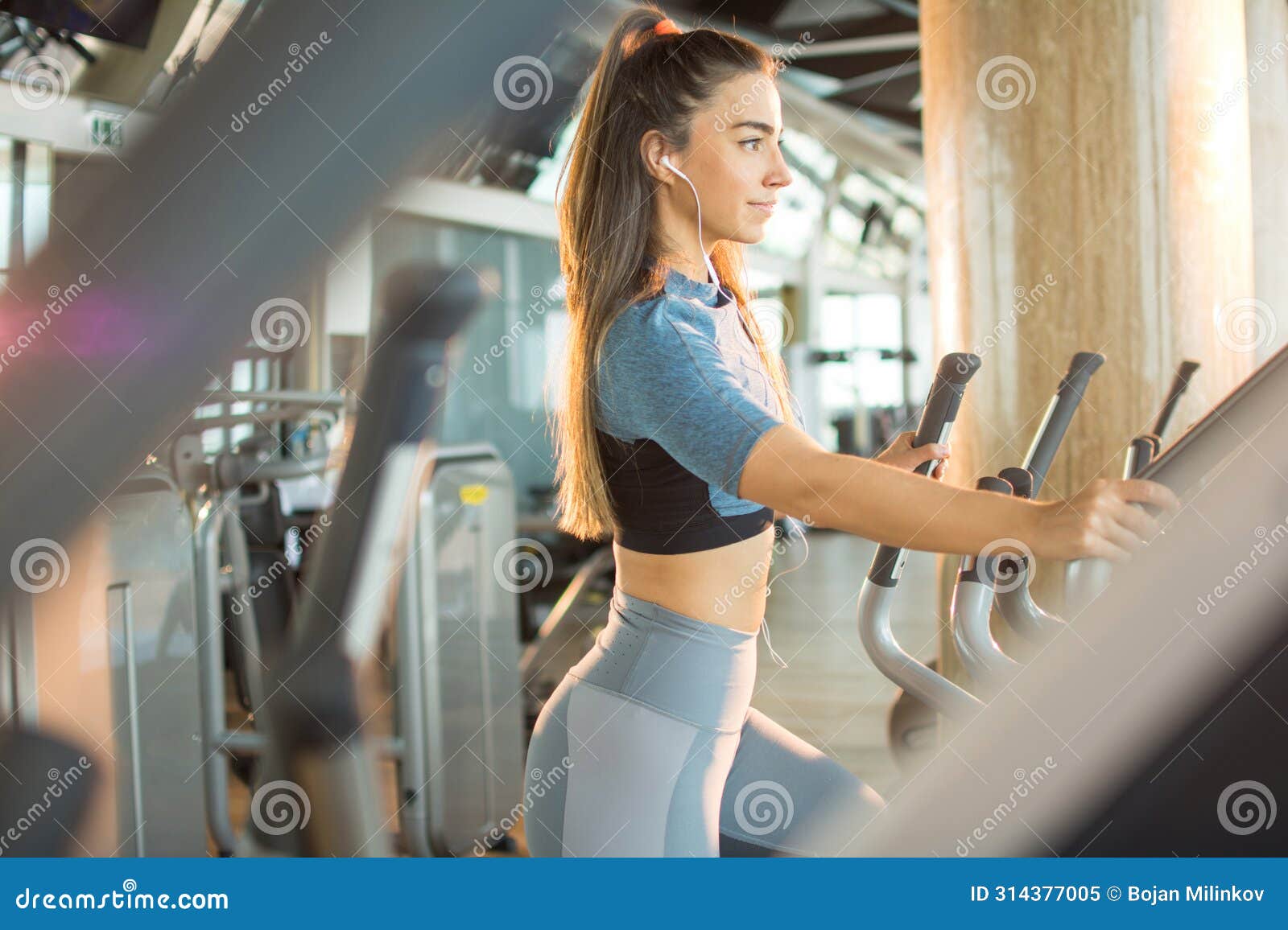 Active Young Woman Exercising on Elliptical Trainer Machine at Gym ...