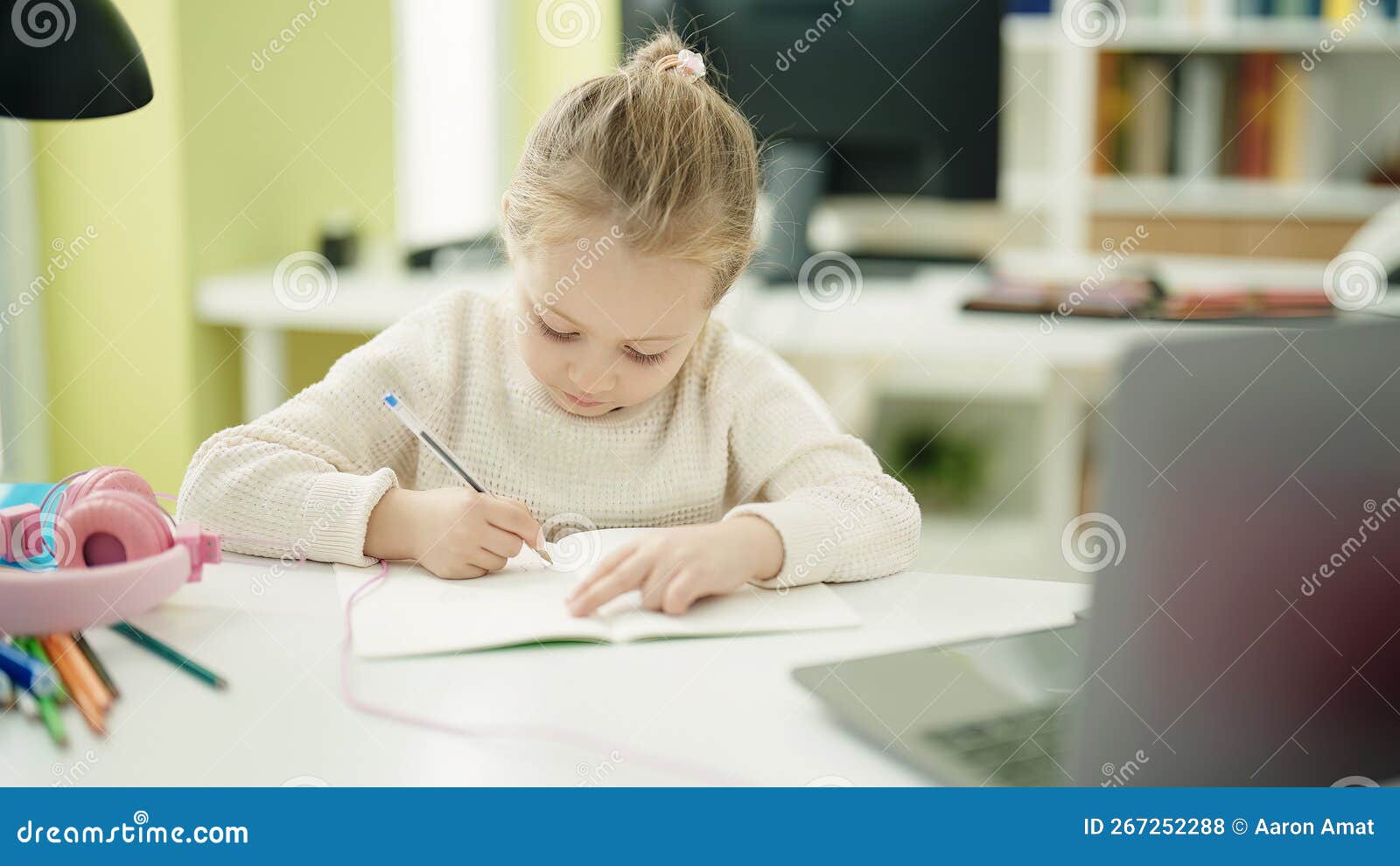 Adorable Blonde Girl Student Writing on Notebook Sitting on Table at ...