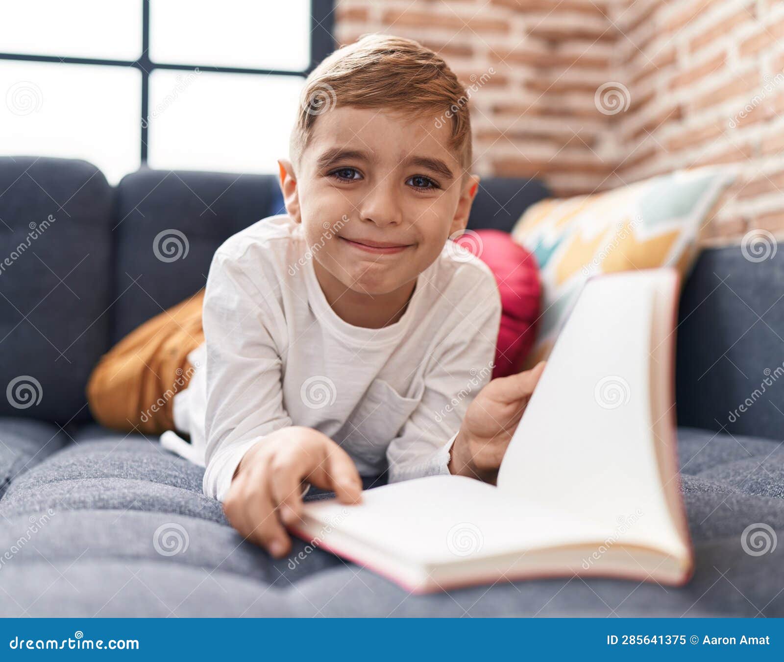 Adorable Hispanic Boy Reading Book Lying on Sofa at Home Stock Image ...