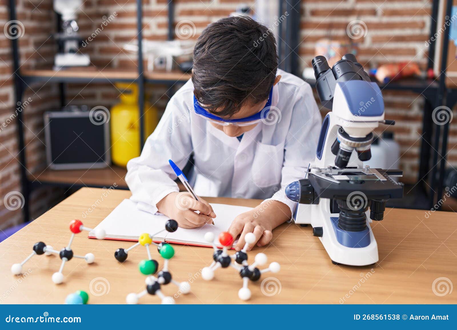 Adorable Hispanic Boy Student Using Microscope Writing on Notebook at ...