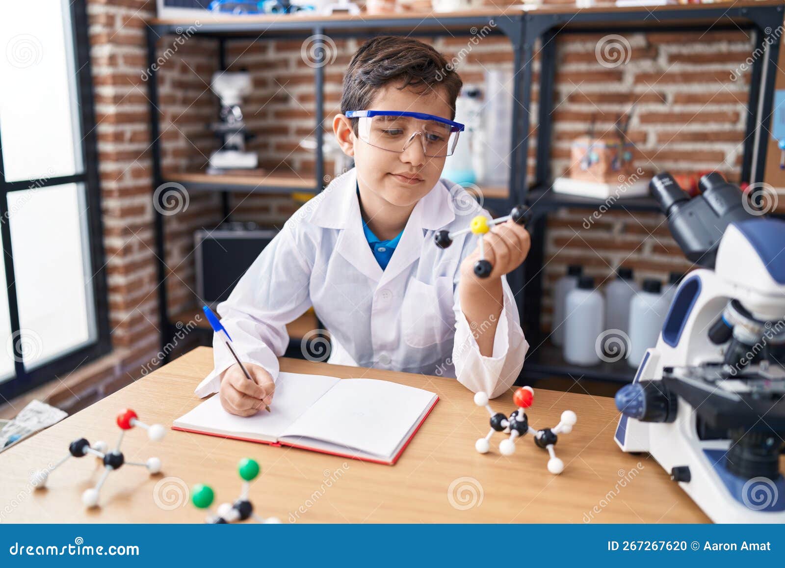 Adorable Hispanic Boy Student Writing on Notebook Holding Molecules at ...