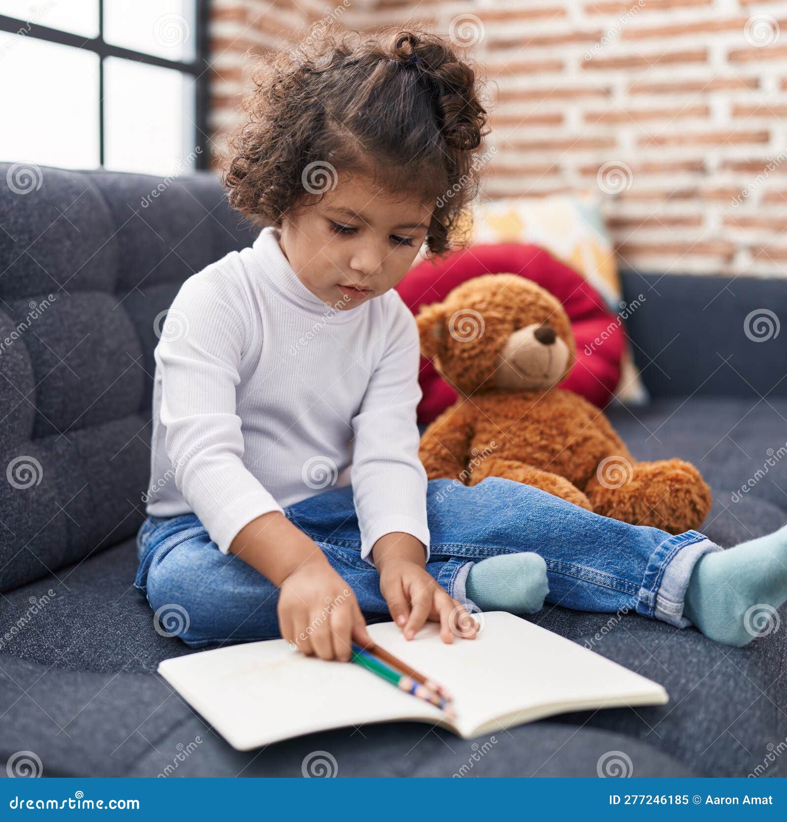 Adorable Hispanic Girl Drawing On Notebook Sitting On Sofa At Home