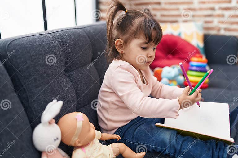 Adorable Hispanic Girl Drawing On Notebook Sitting On Sofa At Home