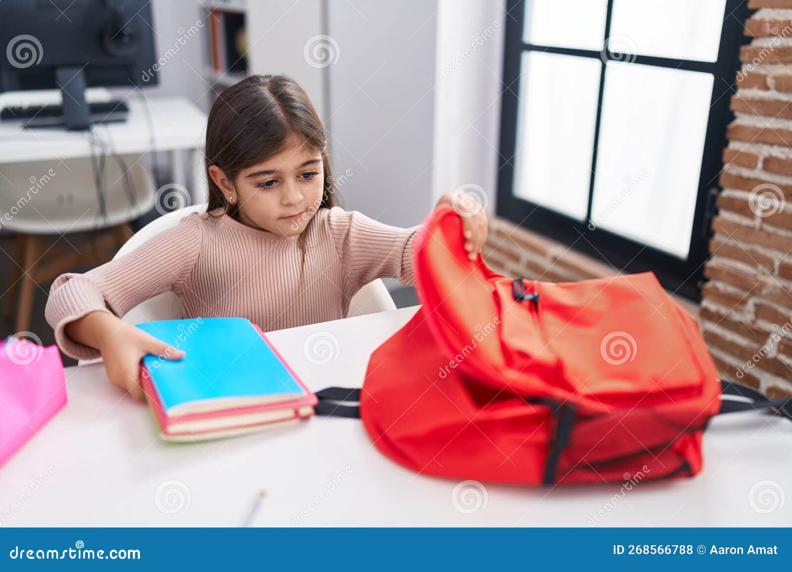 Adorable Hispanic Girl Student Sitting on Table Putting Book on ...