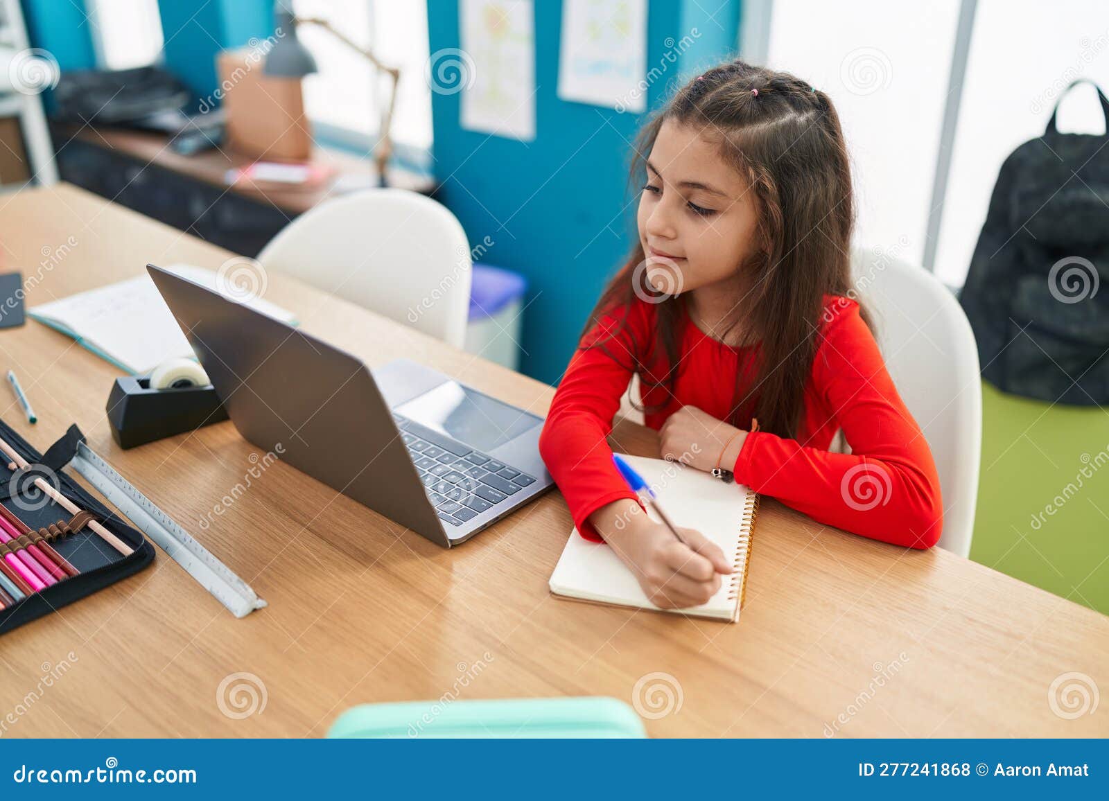 Adorable Hispanic Girl Student Writing on Notebook Using Laptop at ...