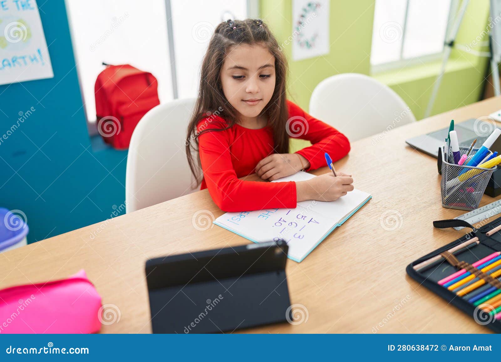 Adorable Hispanic Girl Student Writing on Notebook Using Touchpad at ...