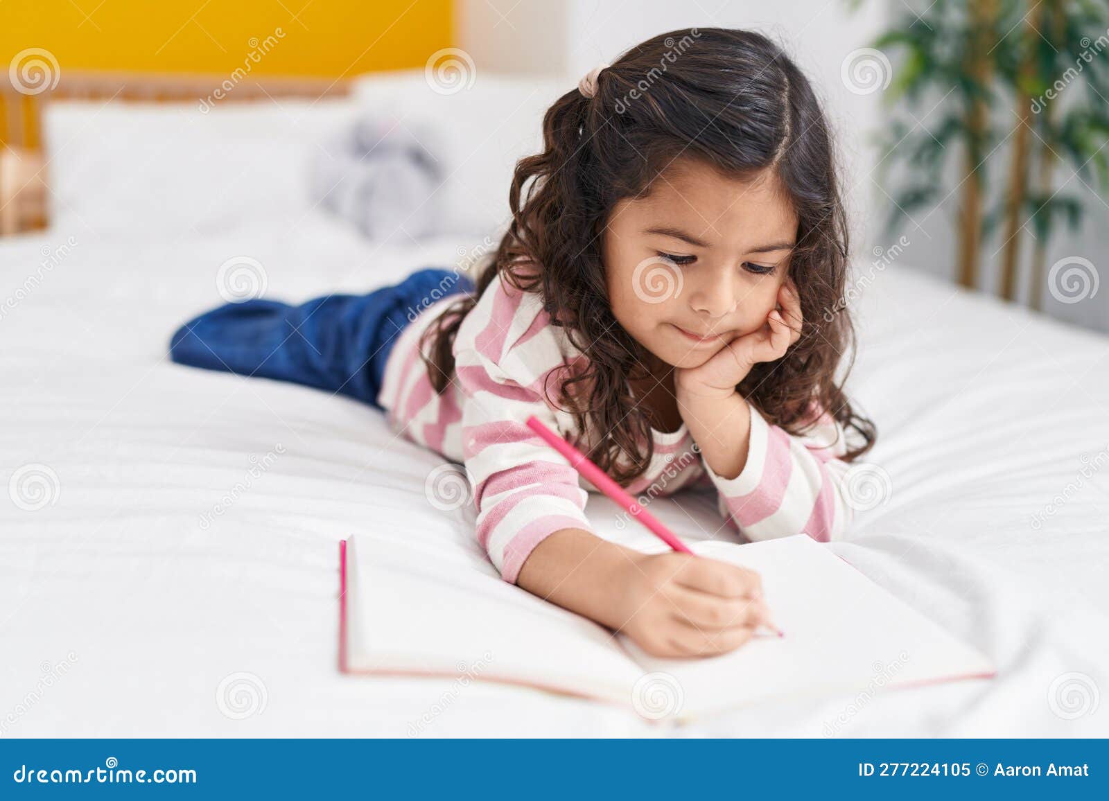 Adorable Hispanic Girl Writing on Notebook Lying on Bed at Bedroom ...
