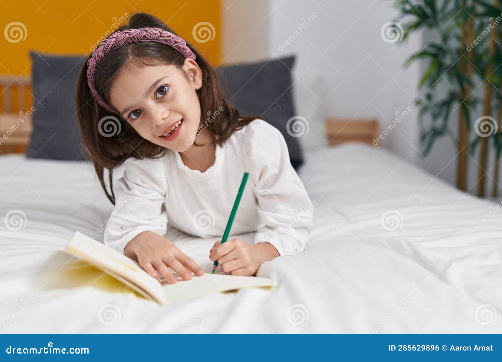 Adorable Hispanic Girl Writing on Notebook Lying on Bed at Bedroom ...