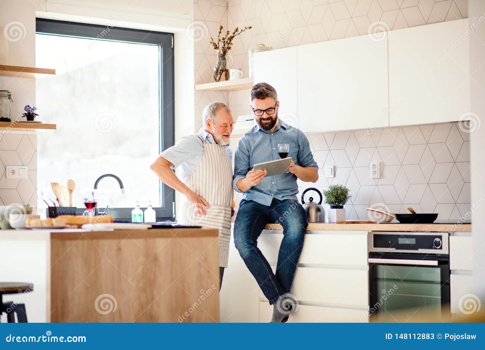 Adult Hipster Son And Senior Father Indoors In Kitchen At Home Using