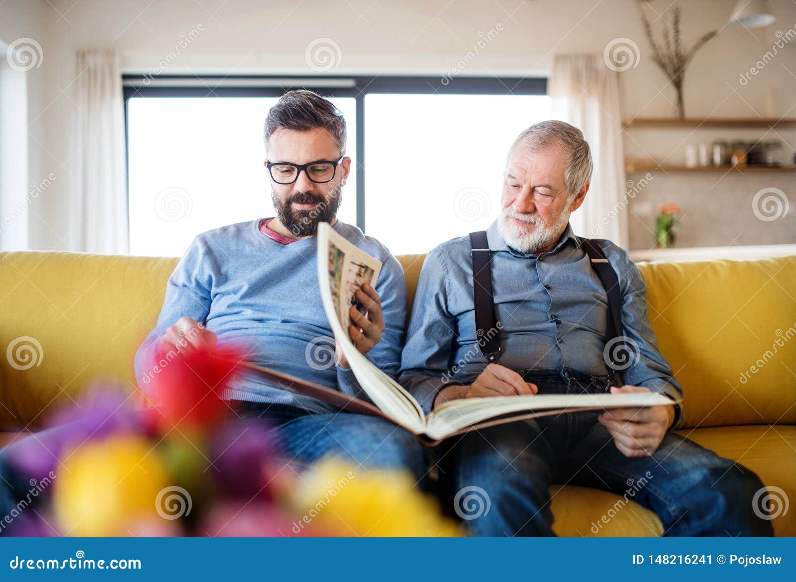 An Adult Hipster Son And Senior Father Sitting On Sofa Indoors At Home