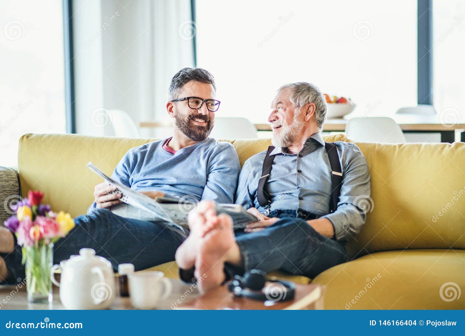An Adult Hipster Son And Senior Father Sitting On Sofa Indoors At Home