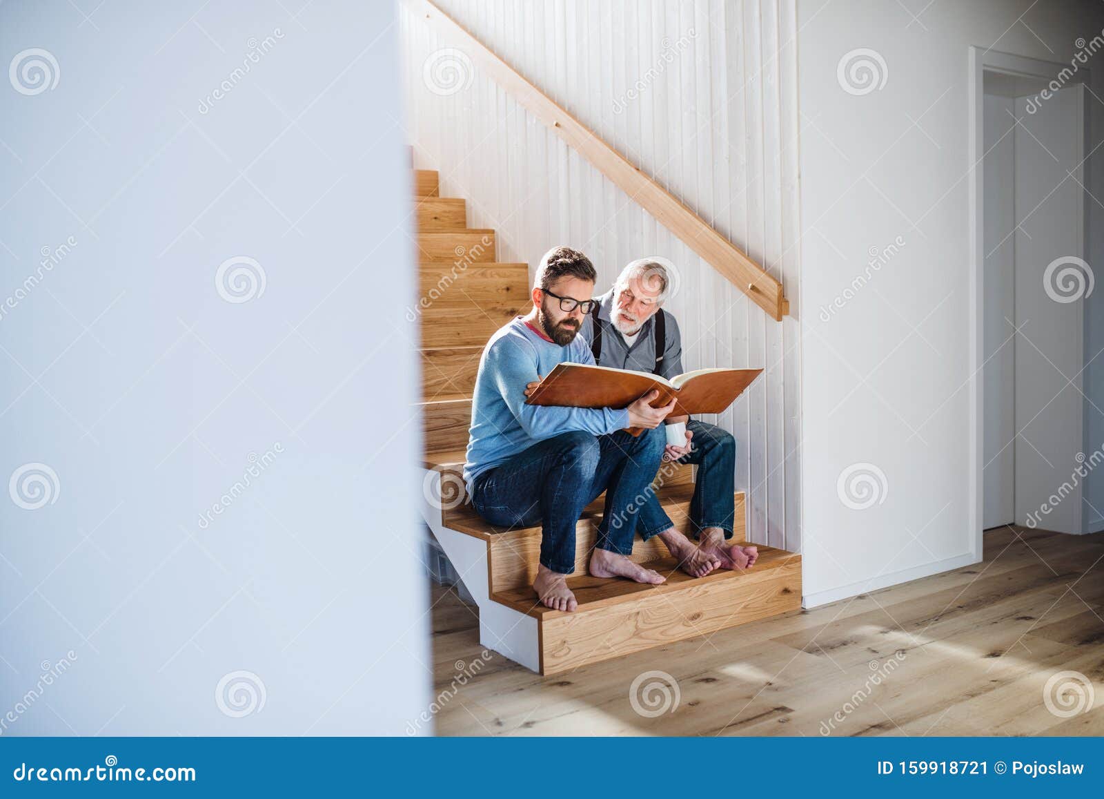 An Adult Son And Senior Father Sitting On Stairs Indoors At Home